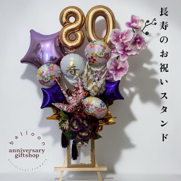 商品説明：節目のお祝いに最適な、豪華なバルーンアレンジメントです。金色のバルーンスウジをメインに、紫を基調としたお花や和柄のバルーンを組み合わせ、華やかさと上品さを演出しました。白色のバルーンには、おめでたい「寿」の文字を金色の筆文字でデザ...