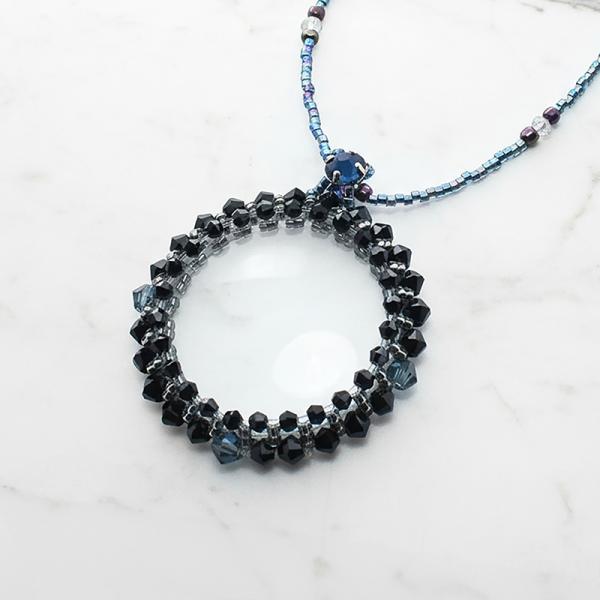 【デザイン】　小さな文字を見る時に便利な、ネックレスタイプのル　ーペペンダント。　ルーペ部分はブラックを基調としたビーズが円形に並　び、華やかな高級感と存在感があります。　ネックレスにはブルー系の小粒ビーズにアクセントで　カラービーズが配さ...
