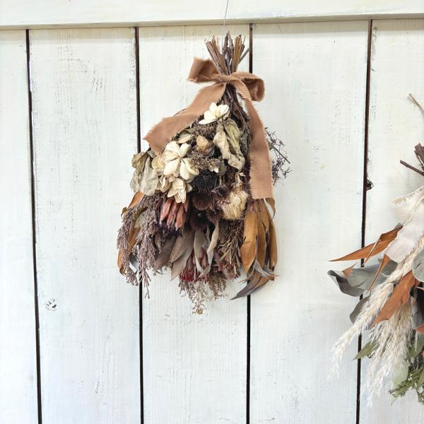 【発売日：2025年06月06日】プロテア・グレビレアなどの人気花材使用。ドライフラワーのスワッグにしてセピアなイメージをお部屋に。一つ一つハンドメイドでおつくりしております。画像のイメージで作成いたします。※映り込んでいる雑貨や什器などは...