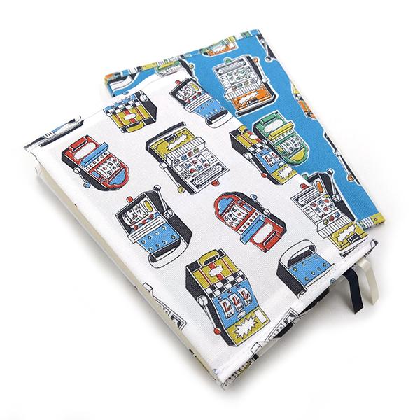 スロット柄の布ブックカバー。内側はPVC加工を施しているので、汚れや水滴から本を守ります。折り返して背表紙の厚みによって調整が可能です。2本のしおり紐付き。素材：綿生産：日本調整幅：1〜3cm程度の背幅に対応使用上の注意：洗濯はできません。...