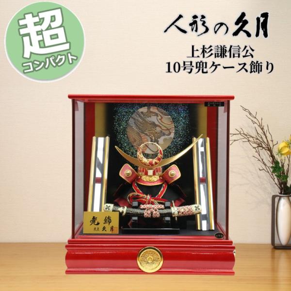 上杉謙信公の兜ケース飾りです。ラメの入った赤塗ケースに弓太刀の変わりに鏡の飾りをあしらった近未来感を感じるモダンなケース飾りです。■特徴ガラスケース（天面のみアクリル）、横太刀付、家紋入れ、オルゴール付き■メーカー人形の久月■サイズ間口×奥...