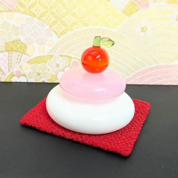 鏡餅（みかん乗せ）ちりめん台付のガラス細工の置物です。【大きさ】約高さ２５ミリ　　横幅３０ミリ　　　　　奥行３０ミリ＊商品は一つ一つ手造りのため大きさや色合いなどが写真と異なる場合がありますのでご了承をお願い致します。