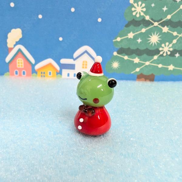 カエルサンタ（リボン）のガラス細工の置物です。【大きさ】約高さ２８ミリ　　横幅１５ミリ　　　　　奥行１５ミリ＊商品は一つ一つ手造りのため大きさや色合いなどが写真と異なる場合がありますのでご了承をお願い致します。