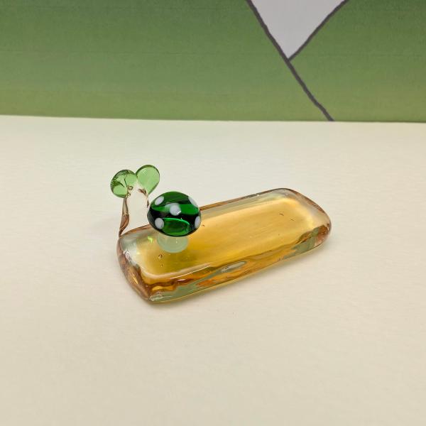 切り株（クリア茶）ときのこ（緑）のガラス細工の置物です。【大きさ】約高さ１５ミリ　　横幅４０ミリ　　　　　奥行１６ミリ＊商品は一つ一つ手造りのため大きさや色合いなどが写真と異なる場合がありますのでご了承をお願い致します。