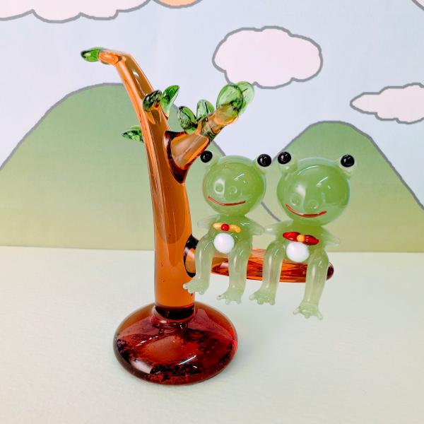 カエルペアと木のガラス細工の置物です。【大きさ】約高さ７０ミリ　　横幅６０ミリ　　　　　奥行３２ミリ＊商品は一つ一つ手造りのため大きさや色合いなどが写真と異なる場合がありますのでご了承をお願い致します。