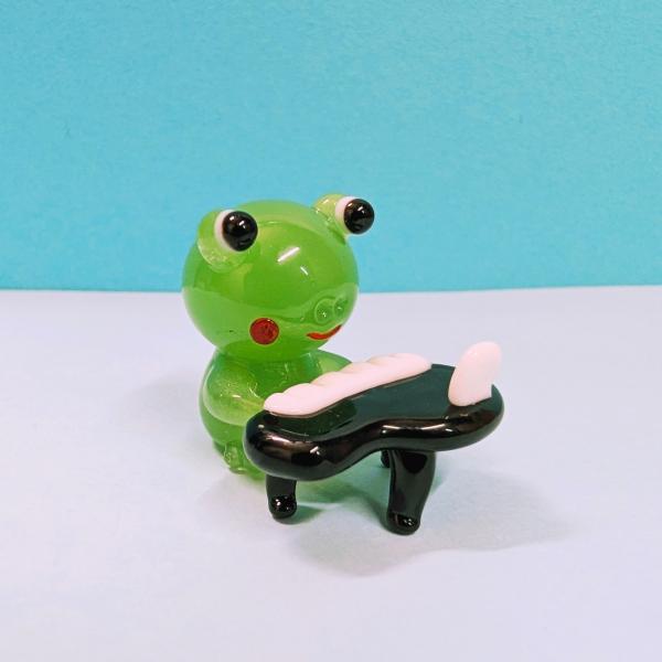 カエルとピアノのガラス細工の置物です。【大きさ】約高さ２４ミリ　　横幅１８ミリ　　　　　奥行１５ミリ　（カエルの大きさ）＊商品は一つ一つ手造りのため大きさや色合いなどが写真と異なる場合がありますのでご了承をお願い致します。