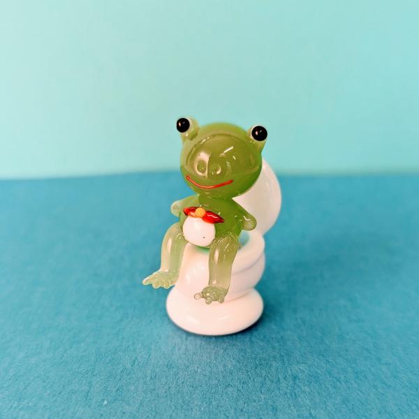 トイレカエルのガラス細工の置物です。＊リボンの色は赤に変わる場合がありますのでご了承をお願い致します。【大きさ】約高さ４０ミリ　　横幅２０ミリ　　　　　奥行２５ミリ＊商品は一つ一つ手造りのため大きさや色合いなどが写真と異なる場合がありますの...