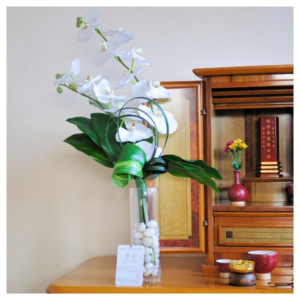 仏壇や遺影に添えるお供え花を造花でアレンジメントしました。高級花の代名詞「胡蝶蘭」を切花でガラス花瓶に挿しました。白の胡蝶蘭は、生花でも時折フューネラル胡蝶蘭としてお供え花に利用されています。豪華で品のある作品に仕上げた当店のオリジナル商品です。