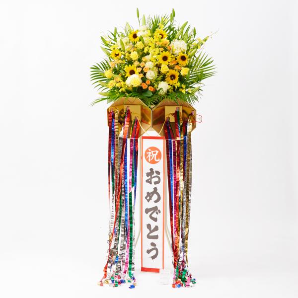 お祝いのシーンを盛り上げる存在感のあるくす玉が付いた、思わず目に留まる派手なスタンド花です。ゴールドのくす玉を割ると、カラフルな銀テープと一緒に「祝おめでとう」と書かれた紅白の垂れ幕が垂れ下がるお祝い花にふさわしい贈答用ギフトです。