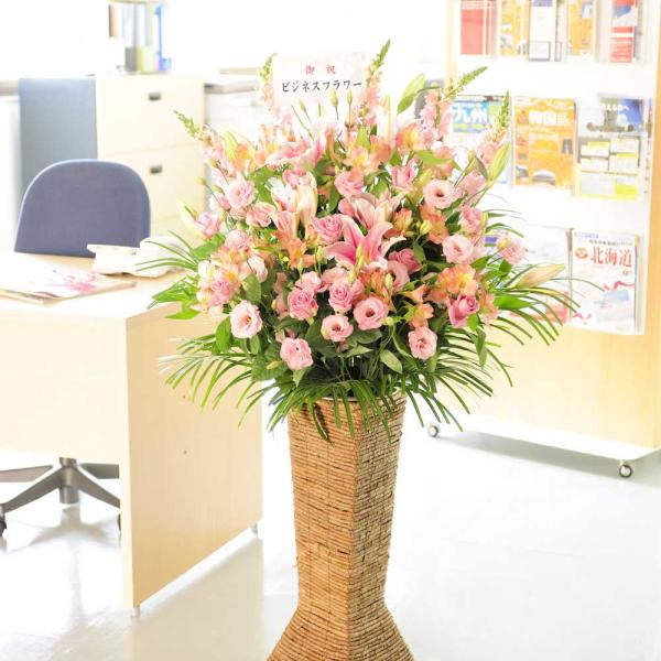 籐かごを思わせるスクエアタイプのスタンド花！（ミディアムスタンド）お花はピンク系をメインに可愛らしく、華やかなに仕立てて届け致します。開店祝いや開業祝いに利用されるスタンドタイプですが他のスタンド花と違い、籐を編み込んだ様な使用となっている...
