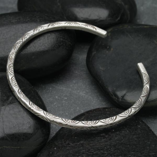 三面に刻印を花びらのように表現した、細身で角棒のカレンシルバーバングルです。装着するとつつましさを感じるほどの細さながらも、目を近づけると精緻かつ味わい深い装飾が広がっています。手作りの上品さと可憐さをあわせ持つデザインです。メンズ/レディ...