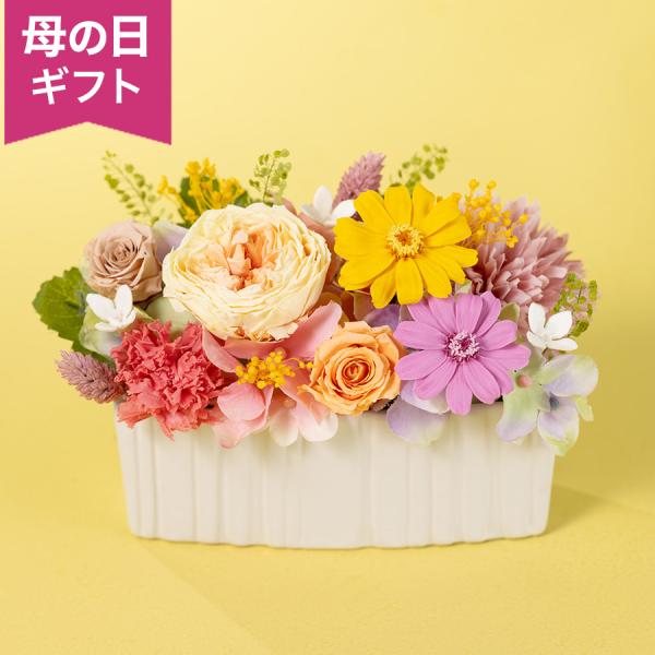 春の光をぎゅっと閉じ込めたようなアレンジメントダイニングテーブルやカウンターに飾りやすい、奥行きを抑えたワイドデザインのアレンジメントです。幾重にも重なる花びらが美しいクラシックローズを主役に、ミニバラや感謝の象徴であるカーネーション、表情...