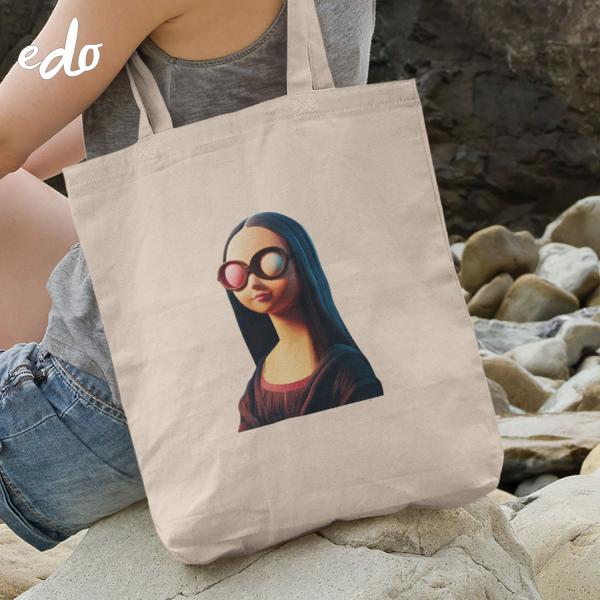 サングラスをかけた女性が微笑む、ユニークでインパクト抜群のキャンバストートバッグ。誰もが知る神秘的な図柄が、ポップで現代的なセンスと融合し、日常にアートを取り入れる楽しさを教えてくれます。シンプルなコーディネートにも映えるこのデザインは、お...