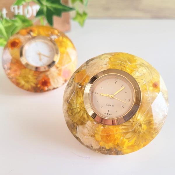 ドライフラワーを全面に詰め込んだ小さな卓上用の花時計です。インアリウムレジン液（エポキシレジン液）を使用しています。本体は、正面から見ると丸い形をしていますが、机と接触する面は多面カットで転がりにくいデザインとなっています。お好きな角度で時...