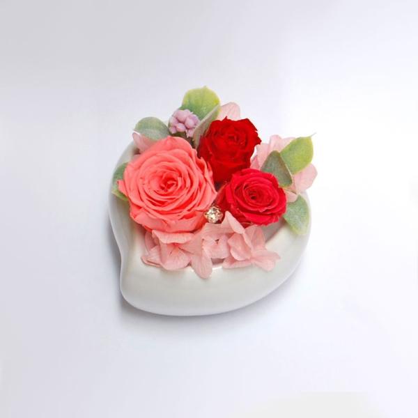 ハート型の丸いフォルムの陶器の花器に、明るく愛らしいピンク色のプリザーブドフラワーが咲くアレンジです。お誕生日のプレゼントやお礼の品など、様々な用途にご利用いただけます。主な花材：薔薇、アジサイ（以上、プリザーブドフラワー）、リーフ（造花）...