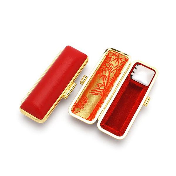 個人印（実印・銀行印・認め印など）を収納する、金色の枠が高級感ある印鑑ケースです。様々なシーンに対応できる、スタンダードな印鑑ケースです。外張りは艶のある赤の合成皮革を使用しています。フタ裏には「朱竹」柄の装飾生地を使用しております。朱肉が...