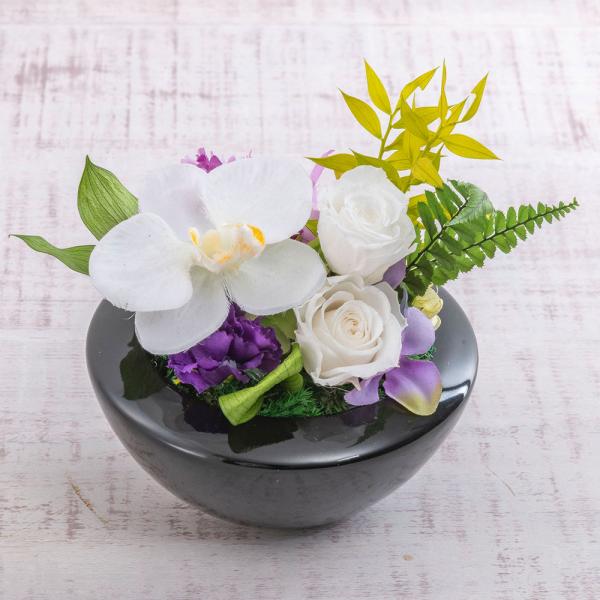 ■お届け 3日後以降でご指定可■注文締切2026/09/27　14:00まで白い蘭とバラが静かに咲き、紫と黄の差し色が故人への想いをそっと照らす仏事用アレンジメント。黒い器の深みが花々の清らかさを引き立て、静寂の中に凛とした気配を宿します。...