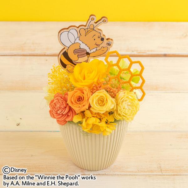 ■お届け 5日後以降でご指定可■注文締切2026/03/26　14:00までみつばちの巣をイメージした、はちみつカラーのお花に、みつばちに扮したキュートな「くまのプーさん」のウッドプレートを添えました。プリザーブド＆アーティフィシャルアレン...