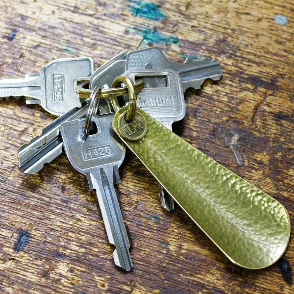 日本の職人が丹念に打ち出し加工を施した真鍮製シューホーン。鍛えることで強度を増したシューホーンは乱反射する黄金色の光をもとうように存在感を放つ。古くから用いられてきた伝統技法をデザインに昇華させた意匠をもつキーリング付きのシンプルなポケッタ...