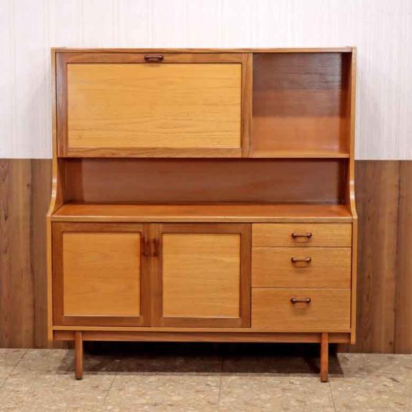 イギリスのミッドセンチュリーモダンを象徴する、温かみのあるチーク材を使用したキャビネットです。上部にはドロップダウン式の扉があり、開くとライティングビューロー（作業スペース）として機能します。内部には収納スペースや棚があり、デスク周りを整理...