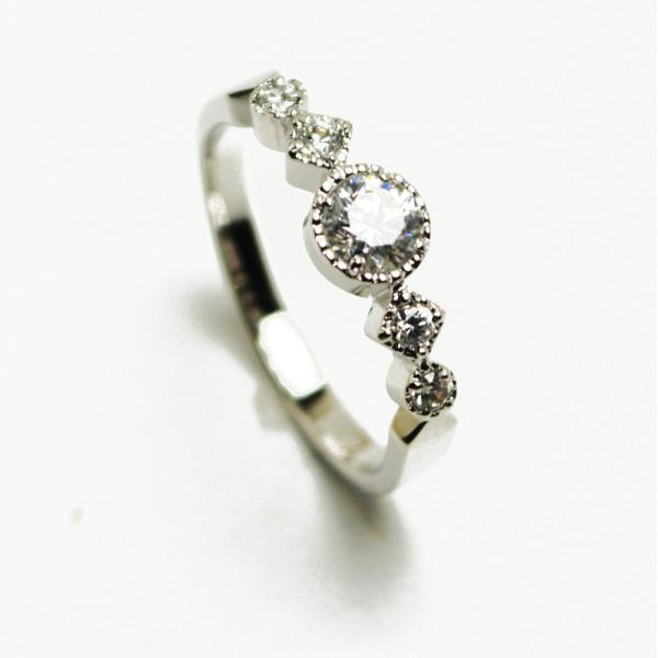 普段使いしたくなる 綺麗なキュービックリングセンターのキュービックジルコニアが大粒で可愛らしいミル打ちの覆輪留めデザインです。脇石も左右に2石づつセッティングしてあります。※サイズ変更の場合、ご注文後にお造り致しますので、10営業日ほどお時...