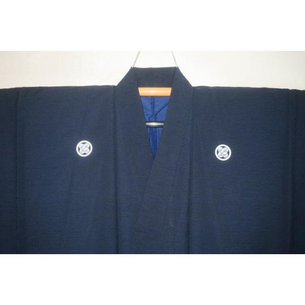 　こちらのお品は、シルク化繊丹後縮緬調のお召の袷の着物に紋を入れたものです。元の着物はミシン手縫い併用の呉服仕立ての新品です。紋付の着物のみです。化繊の染物調ですが、本絹並みです。むしろ本絹より扱いやすいかもしれません。藍色の無地感です。裏...