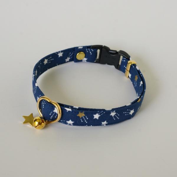 尾を引く流れ星が可愛いデザインの猫用首輪です。ネイビーブルーの地に、白の星と点線の尾の流れ星がいっぱいプリントされています。【素材】■首輪ベルト部分：コットン100%■美錠・サルカン・カシメ・鈴・星形チャーム：金具（メッキカラー：ゴールドo...