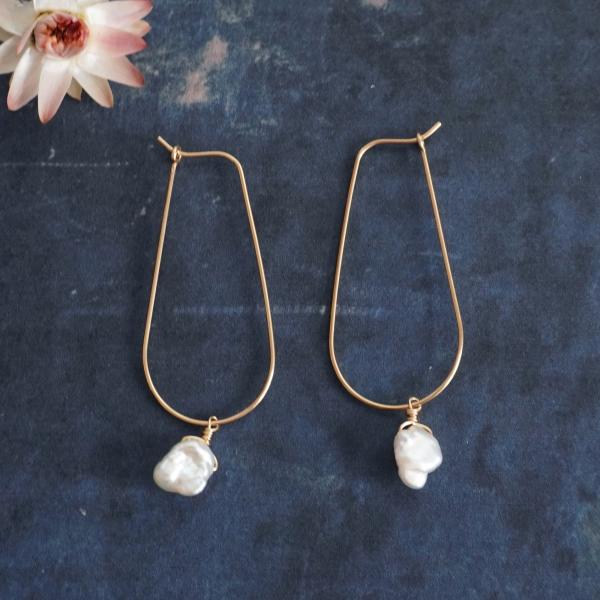 ゴールドフィルドワイヤーで作られたロングフープに自然が生み出した花びらのようなフォルムのケシパールが１粒あしらわれたピアスです。パールにはとても美しい照りが見られます。全ての金具にゴールドフィルドを使用。高級感があり、金属アレルギーの方にも...