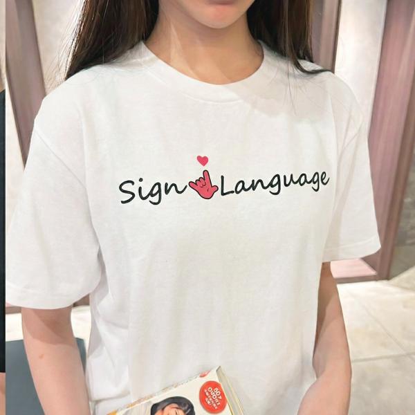 「Sign Language（手話）」の文字とともに、ピンク色の手話「I Love You」サインが可愛らしいハートマーク付きでデザインされています。見る人の心をほっこりさせる、シンプルながらもメッセージ性の強い一枚です。・素材：綿 100...