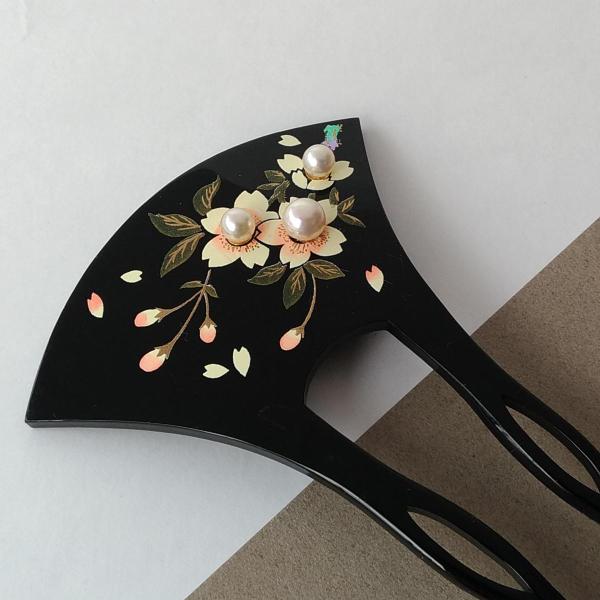 本真珠をあしらった扇形・蒔絵風かんざしです。お着物に華やかな色どりを添えてくれます。パールが控えめに輝く、端麗かつシックな逸品。和の装いに１つあると大変重宝です。真珠：6.7mm×1個,  5.3mm×2個台　：プラスチック（黒）　大きさ：...