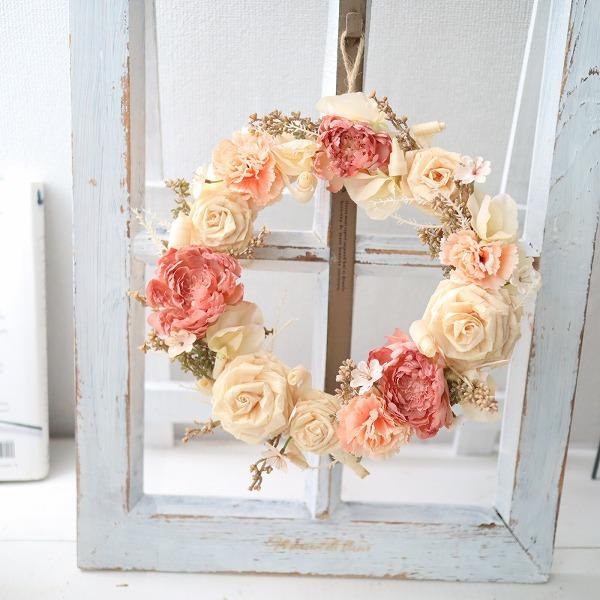 土台にもかんなくずを巻きつけ、ナチュラルで優しい風合いに仕上げました。主役は、ヒノキのかんなくずをバラの形に象った、ユニークで美しいお花たち。見る角度によって表情を変え、素朴ながらも洗練された存在感を放ちます。そこに、淡いピーチピンクのラナ...