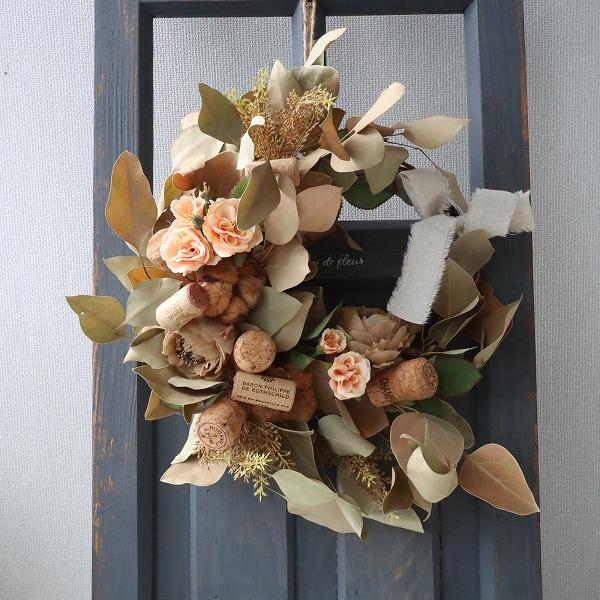 アンティークな風合いが魅力的な、造花とドライフラワーを組み合わせたリースです。落ち着いたベージュ、ブラウン、コーラルの色合いでまとめ、秋冬のインテリアに溶け込むようデザインしました。ポイントとして、ワインコルクをあしらい、大人っぽくも遊び心...
