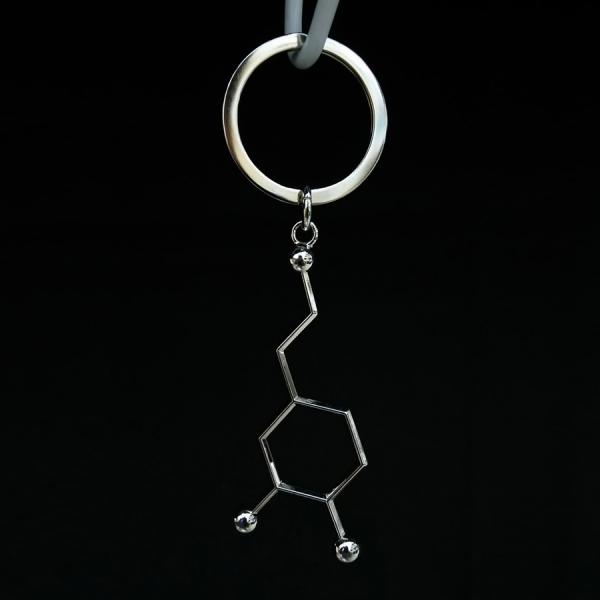 ドーパミン(dopamine)の分子構造をしたキーホルダー。中枢神経系に存在する神経伝達物質で、報酬系に重要な役割を果たし、意欲、動機、愛情などに関わる。サイズ：長さ約2.4インチ（6センチ）。約9グラム材質：合金（alloy metal）製