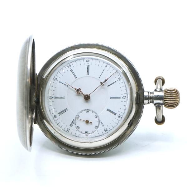 明治時代、商館と呼ばれる外国の商社が社名を入れて日本に輸入したのが商館時計と呼ばれています。この形状はフルハンターケースで、狩猟の際に風防が割れないように時計の表と裏の両側が蓋で覆われたことから来ています。提げ環に2か所鍔が付けてあるのは、...