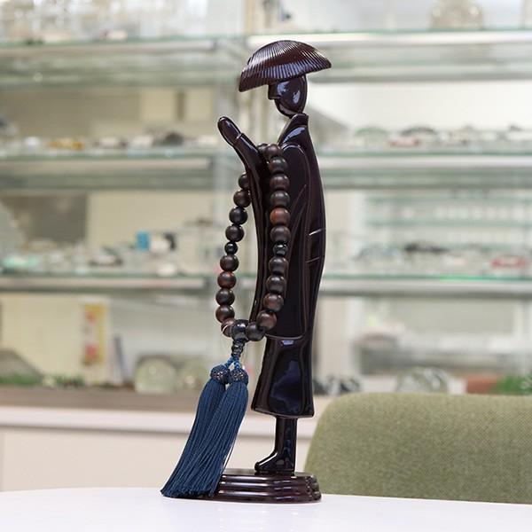 数珠を掛けて頂ける数珠掛けでございます。托鉢像をモチーフにしておりますが、托鉢（たくはつ）とは、修行僧が修行のため、鉢(はち)を持って、家の前に立ち、経文を唱えて米や金銭の施しを受けて回ることを意味しております。尊いお数珠を大切にして頂ける...