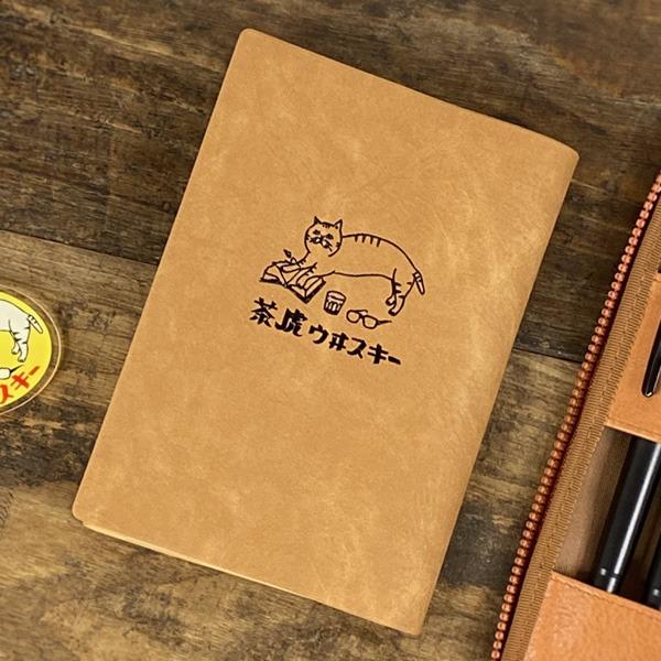 ふわっとした手触りの渋いカラーの合皮素材に茶虎ウヰスキーのロゴを施した文庫本用ブックカバーです。ひとつずつニュアンスの異なるPVC（合皮素材）を採用しているため、1点ずつ箔押しをする過程で若干のかすれや跳ねが生じます。PVCのニュアンス次第...