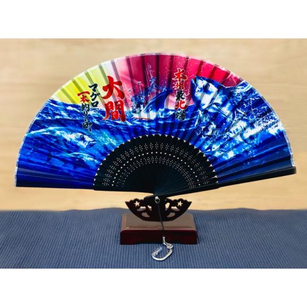 大間の荒れ狂う海と巨大なマグロそしてそのマグロに立ち向かうマグロ漁船のデザイン漢のロマンがたっぷり詰まった扇子です♪持ち運びにも便利なサイズ感ディスプレイ用として飾ってもGOOD!！本物のマグロ針を持ち手の下部分に付けたデザインです。※危な...