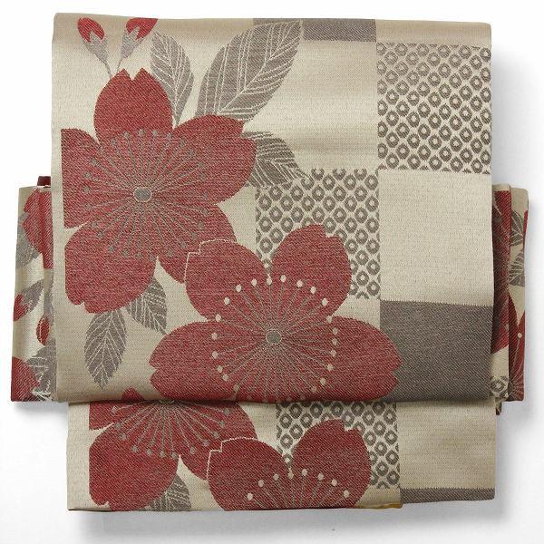 光沢のあるベージュ地に赤く大きな桜を織り出しました。背景には市松文様を疋田調で描いています。モダンデザインのオシャレな京袋帯です。