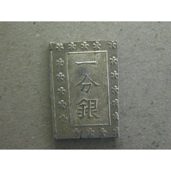 品位　銀８７３／その他１２７　量目８．６３ｇ　天保一分銀と比べますと、切り方が荒く、それが安政一分銀の特徴にもなっています。また、「是」字の第８画と９画が交叉しておらず、人になっています。側面の仕上げは、概して荒いやすり目が入っています。（...