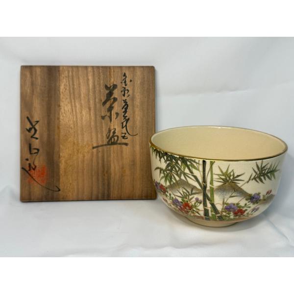 京焼の作家 暁山による京薩摩の茶碗です 未使用の経年在庫品として保管されていたお品です クリーム色の肌に美しい貫入が入り 金彩を用いた竹と可憐な草花が繊細に描かれています 京薩摩ならではの雅で温かみのある佇まいです 高台と共箱に銘がございま...