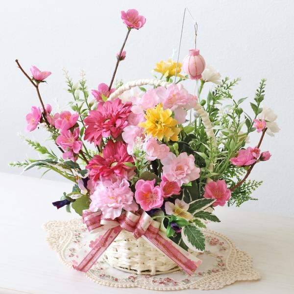 白いのかごに入った、桃と桜とヤグルマギクが優しい色合いのひなまつりアレンジです。サイズ：約高さ27cm×幅28cm×奥行20cm＊商品の仕様は変更になる場合がございます＊受注制作のため数日お時間をいただく場合がございます