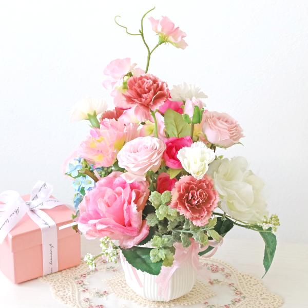母の日に贈る、人気のカーネーションとバラに、ころんとしたチューリップ型の陶製鉢を使用したアレンジメントです。ありがとうの気持ちが伝わるやさしいピンクやホワイトの色合いと、可憐なリボンでとびっきりかわいらしく仕上げました。アレンジメントサイズ...