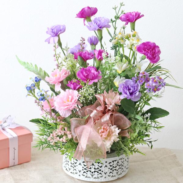 母の日に贈る、ホワイトの器に色とりどりのカーネーションが咲いたアレンジメントです。レース調の模様が目を引くワイヤー製の器は、割れないため倒れても安全です。小ぶりなカーネーションや繊細な葉、やさしげな小花で可憐なアレンジメントに仕上げました。...