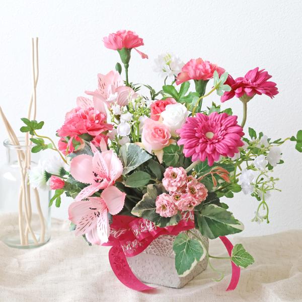 母の日に贈る、ガーベラやアルストロメリア、カーネーションを使ったアレンジメントです。定番のピンクカラーの花々を母の日のリボンでまとめたアレンジは、日頃の感謝の気持ちを贈るプレゼントにぴったりです。アレンジメントサイズ：約高さ28cm×幅32...