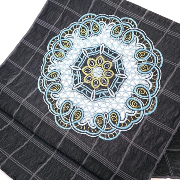 華やかで可憐なレース刺繍を思わせる水色と黄色の華丸モチーフ。刺繍ならではの立体感と繊細さが際立つ作品です。三重織で揺らぐ経糸が透けて見えるおしゃれな帯。地色の墨のようなやや灰みのある黒色は強い色ではないので、軽やかにコーデを引き締めてくれま...