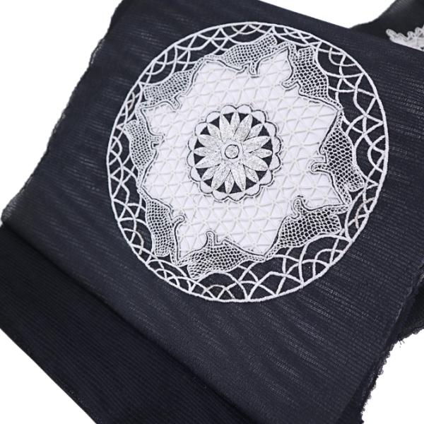 三重織りで揺らぐ経糸が透けて見えるおしゃれな帯。地色は濃色のネイビー。白の刺繍糸が美しく映えるお色です。やや透け感のある帯地はごく薄い緑色で爽やかに。帯の地紋に紋様が織り込まれているので柄の無い部分もおしゃれになっています。可憐なレース刺繍...