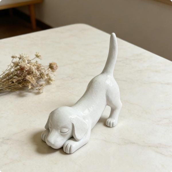 【デザイン】: 伏せポーズの犬をテーマにしたリング付き犬フィギュアで、玄関飾りや棚上のアクセントとして置くだけで空間にやさしい表情を添えます。【用途】: 室内装飾として使いやすい犬の置物で、玄関・リビング・デスク・シェルフなど、さりげなく雰...