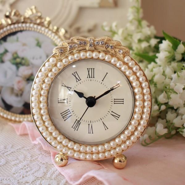 [商品説明]上部のエレガントなリボンモチーフが素敵なアンティーク風の置時計２色展開でこちらはゴールドとなります上品な２連のパールが品良く美しいお品です文字盤はローマ数字でアンティークな雰囲気も漂います秒針音は無音ではございませんが静かな方で...