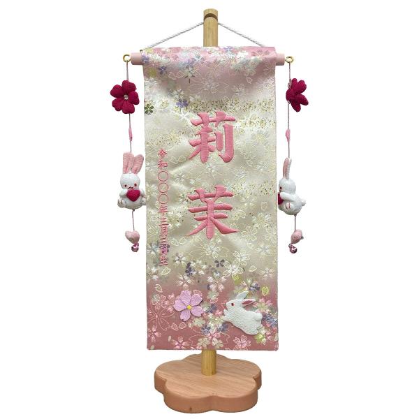 桜花地の生地はホワイトからピンクへの綺麗なグラデーション。その上にちりめん押絵の兎と花があしらわれています。両脇にはかわいい白うさぎ、台座は梅の花をかたどった豪華な仕様の名前旗です。・高さ39cm、間口20cm（房含まず／布13cm）・台座...