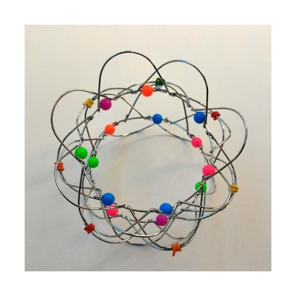 針金が複雑に組まれた幾何学的オブジェです。曲げたり伸ばしたり回したりすると変形して，いろいろな形になります。花，王冠，ステンドグラスのような模様にも見えたりします。うまくたたむとペチャンコにすることもできます。直径約１０センチ。対象年齢６歳...